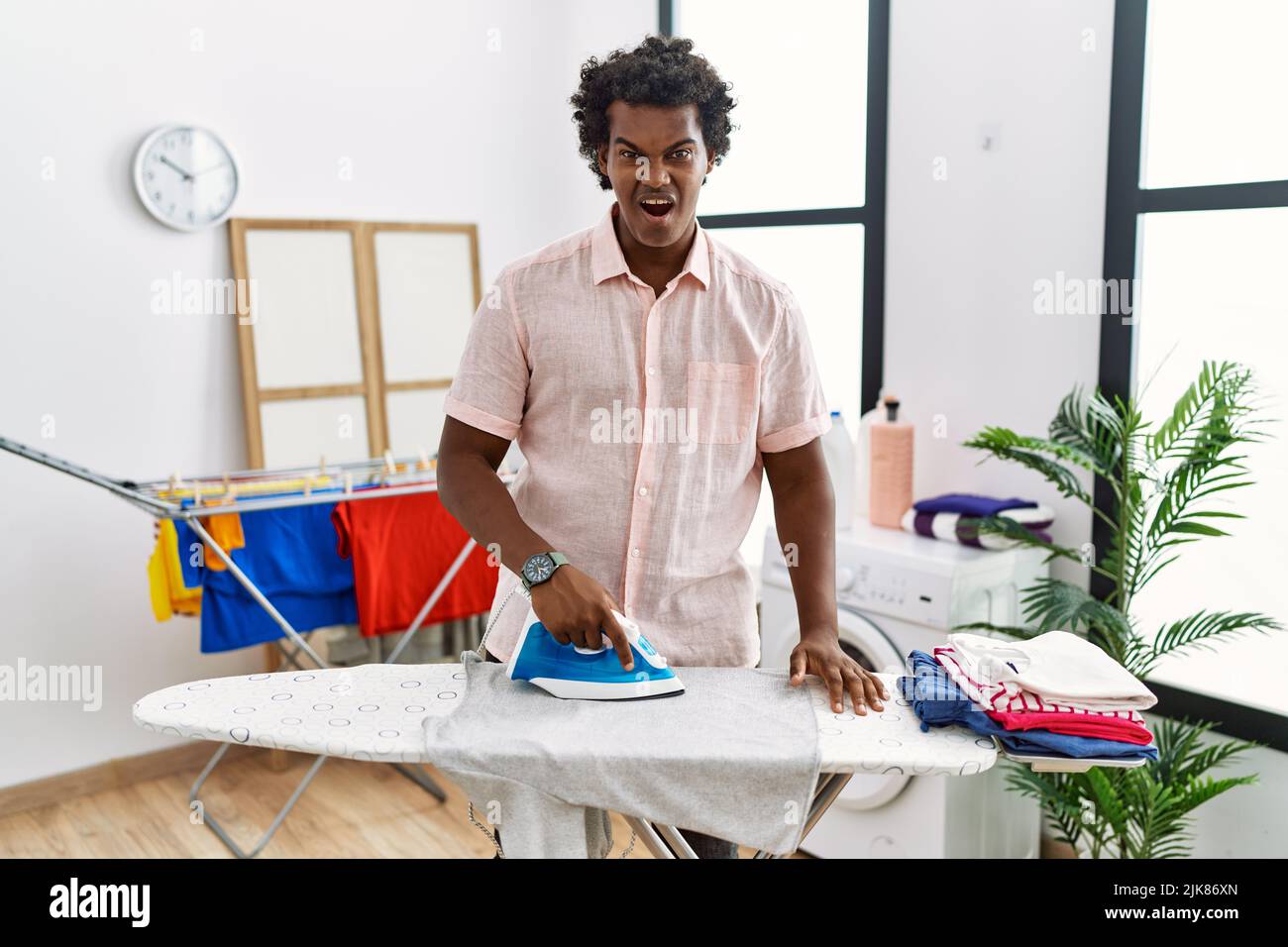 African man with curly hair ironing clothes at home angry and mad ...