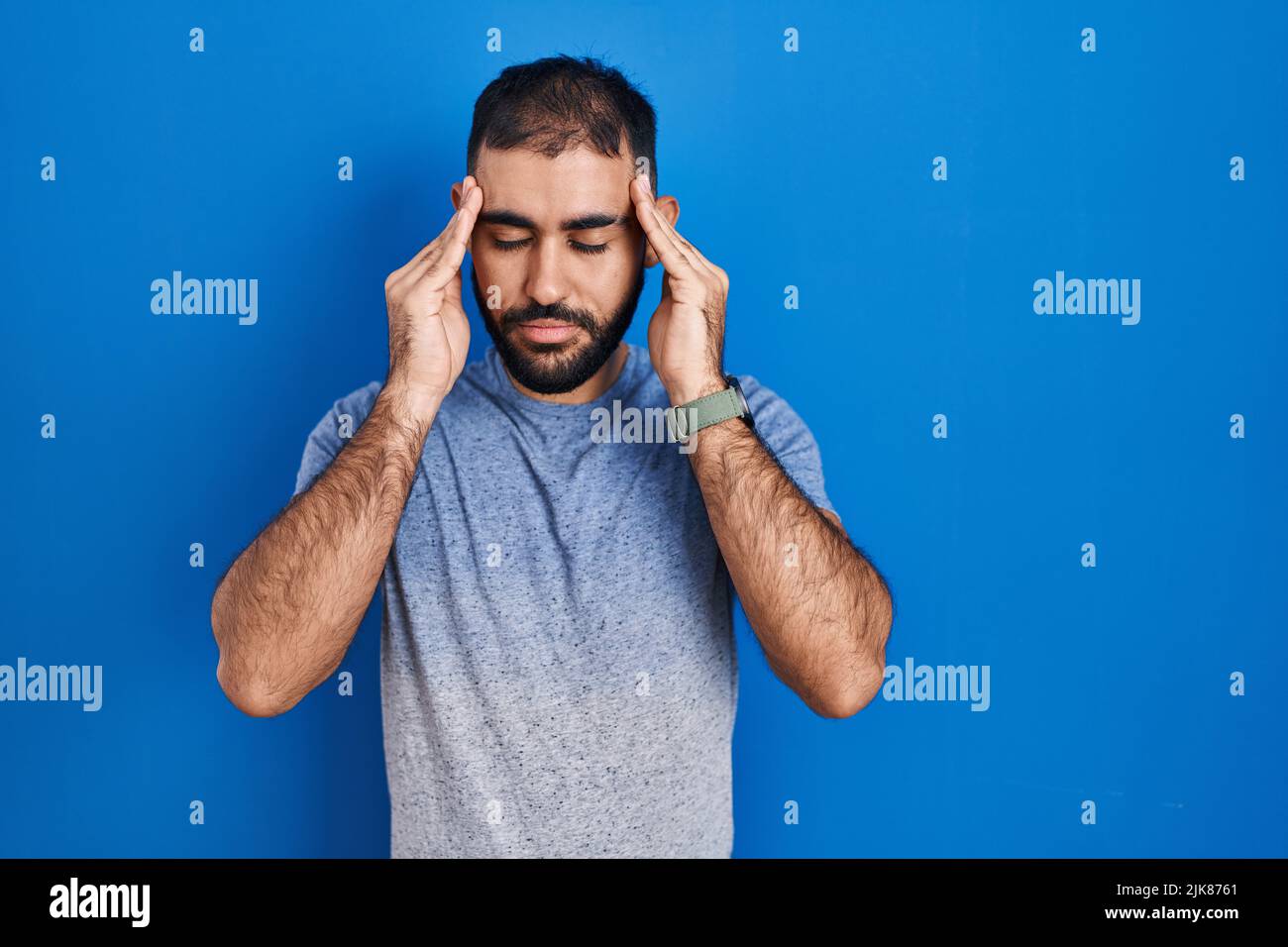 Middle east man with beard standing over blue background with hand on ...