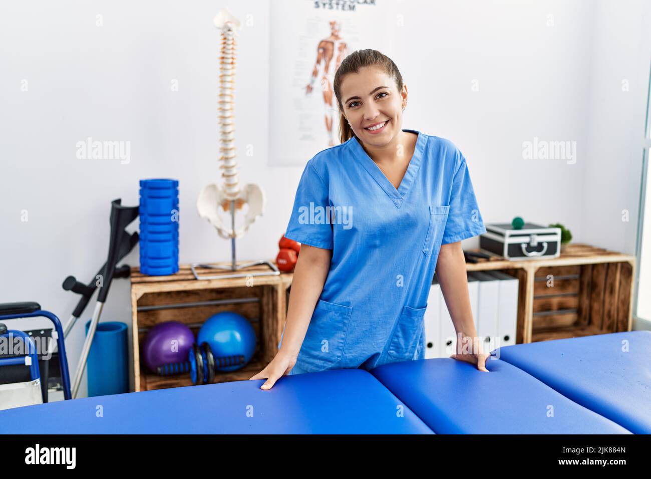 Young hispanic woman wearing physiotherapy uniform standing at sport ...