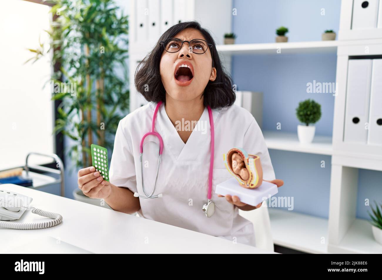 Young hispanic doctor woman holding anatomical model of uterus with ...