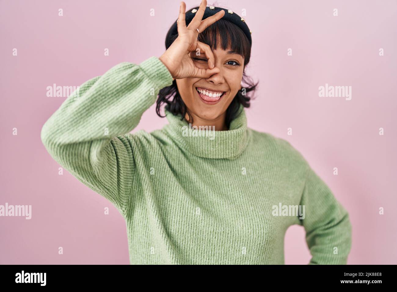 Young beautiful woman standing over pink background doing ok gesture ...