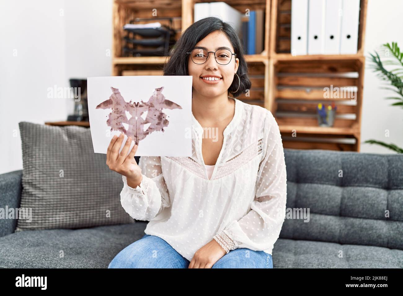 Young hispanic therapist woman holding rorschach test looking positive ...