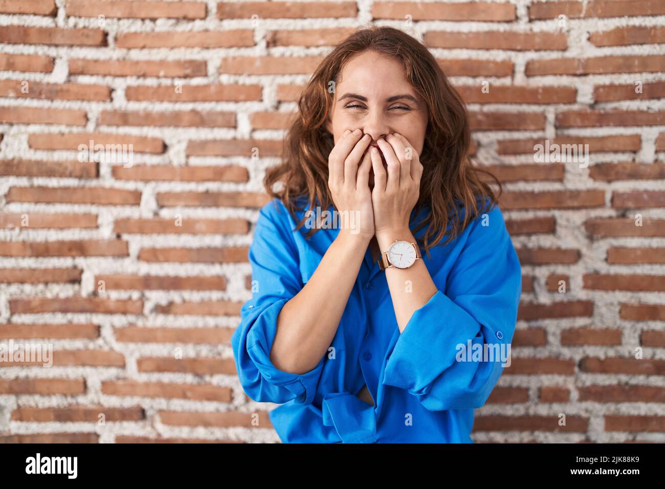 Beautiful brunette woman standing over bricks wall laughing and ...