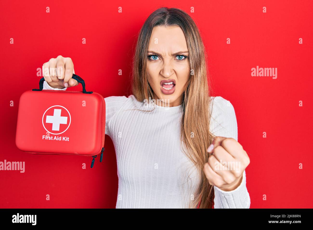 Young blonde girl holding first aid kit annoyed and frustrated shouting ...