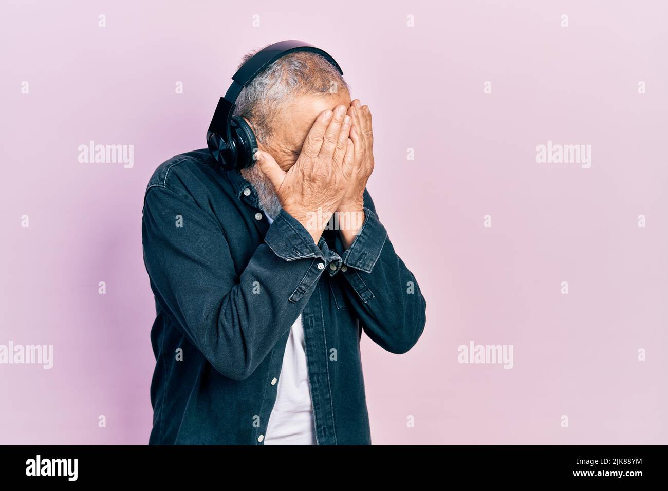 Handsome senior man with beard listening to music using headphones with ...