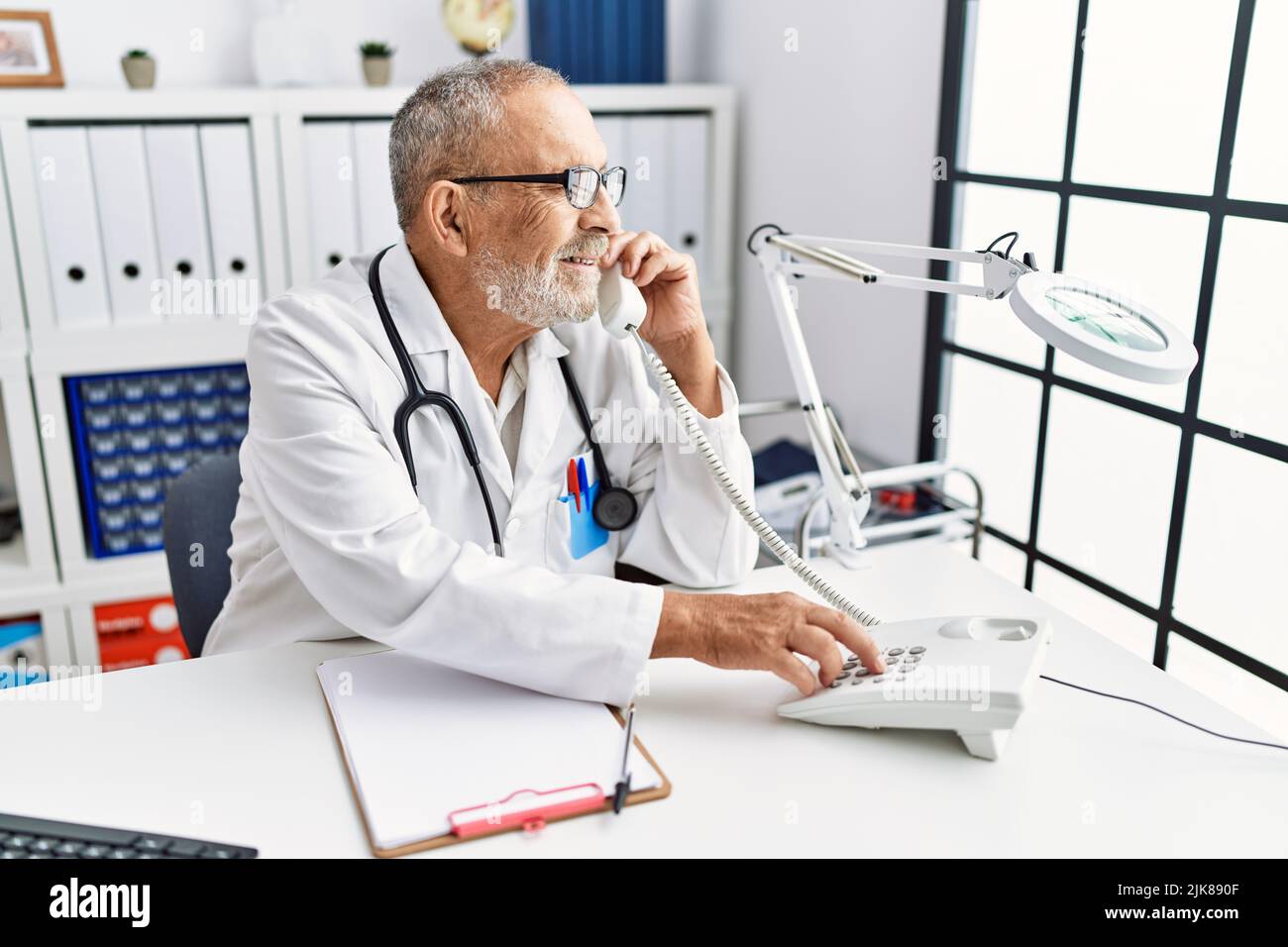 Senior grey-haired man wearing doctor uniform talking on the telephone ...
