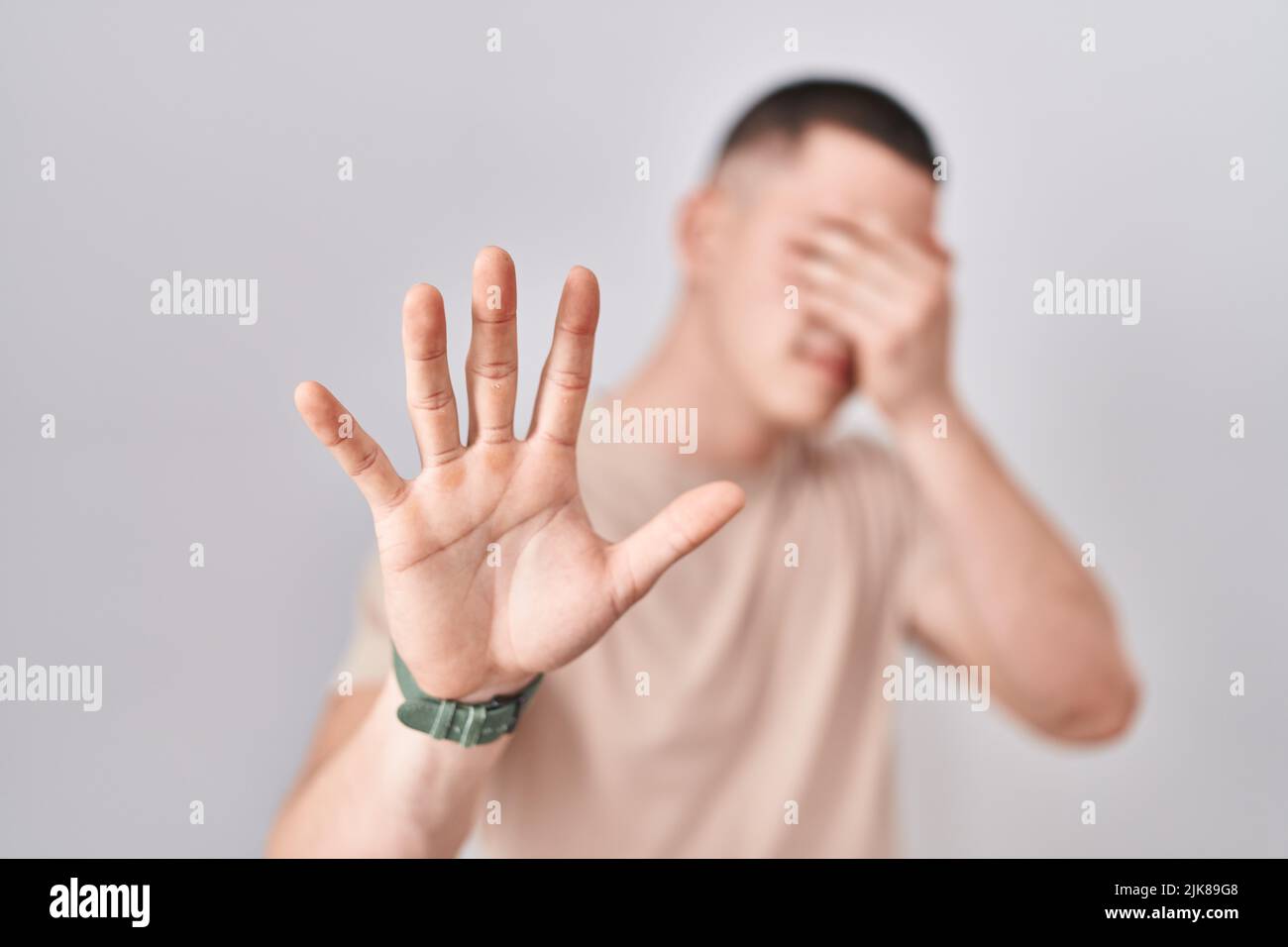 Young man standing over isolated background covering eyes with hands ...