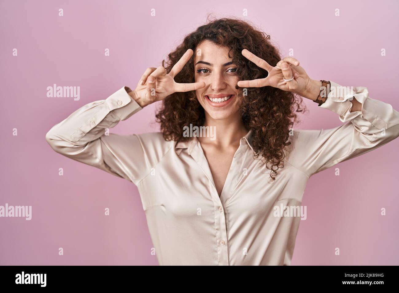 Hispanic woman with curly hair standing over pink background doing ...