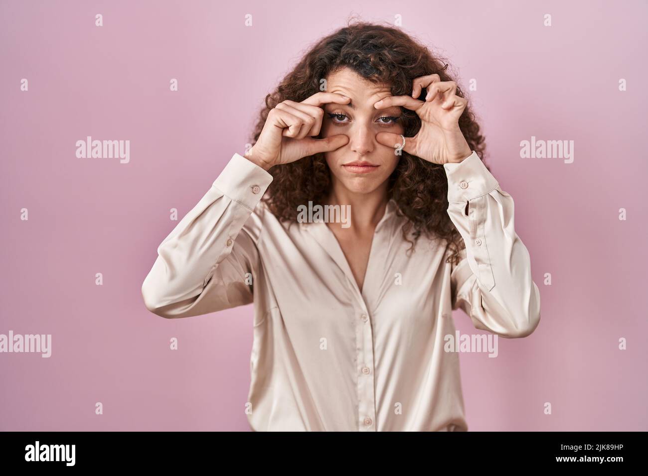 Hispanic woman with curly hair standing over pink background trying to ...