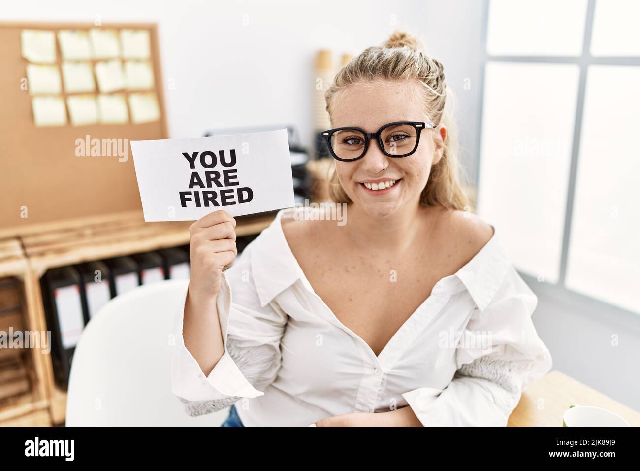 Young caucasian woman holding you are fired banner at the office ...
