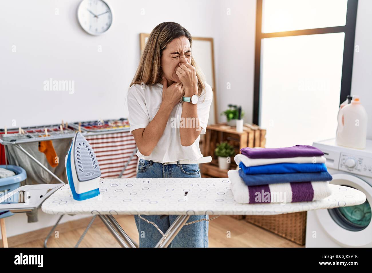 Young hispanic woman ironing clothes at laundry room smelling something ...