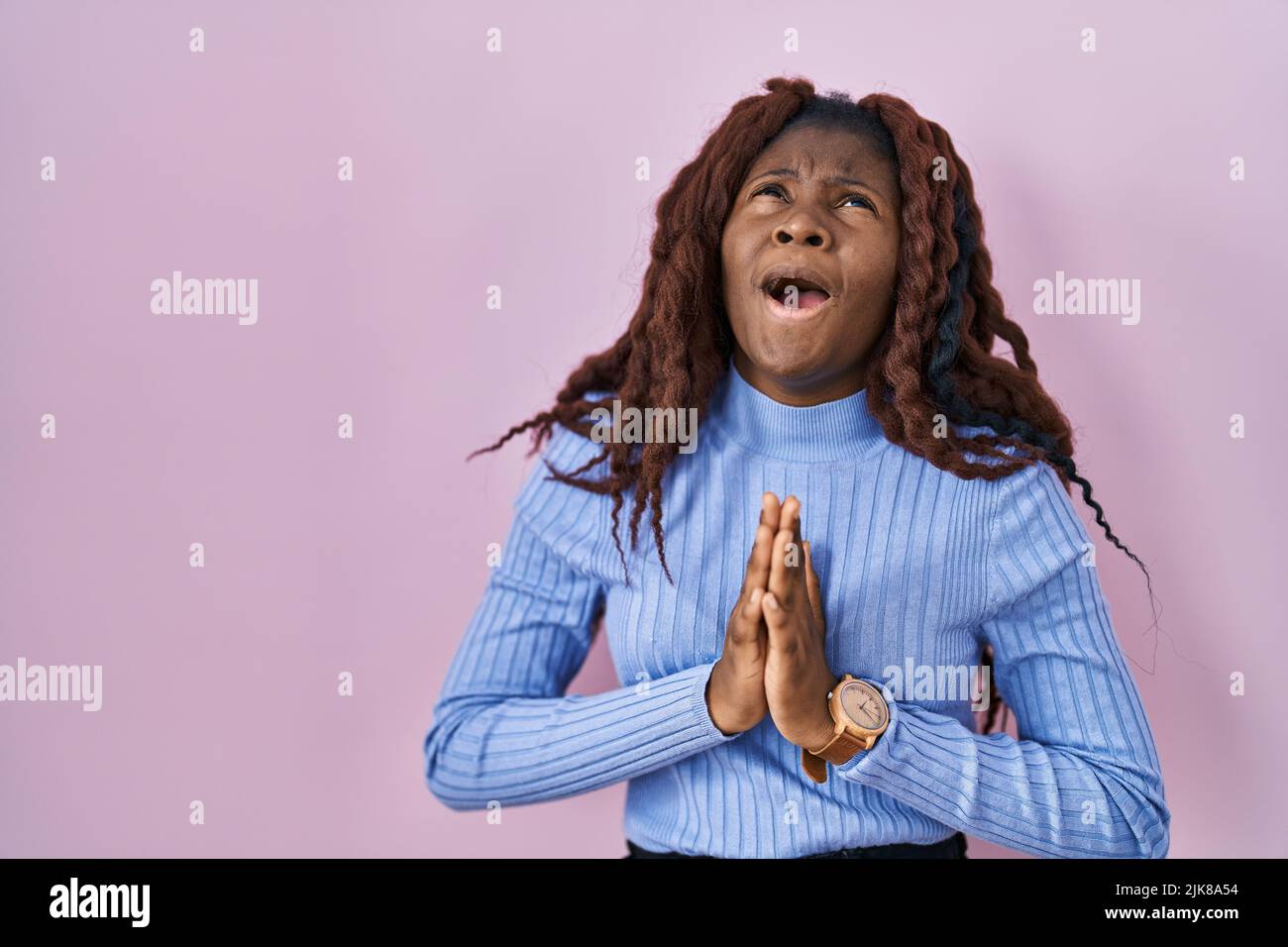 African woman standing over pink background begging and praying with ...