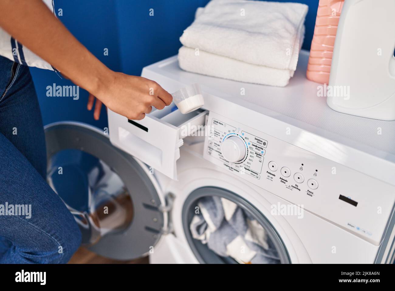 Young blonde woman pouring detergent on washing machine at laundry room ...