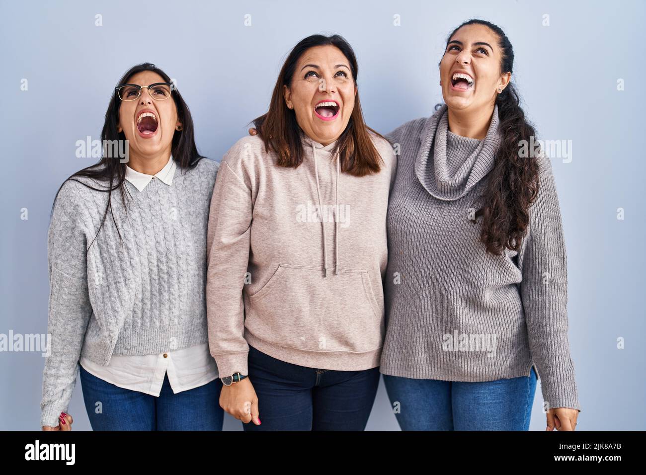 Mother and two daughters standing over blue background angry and mad ...