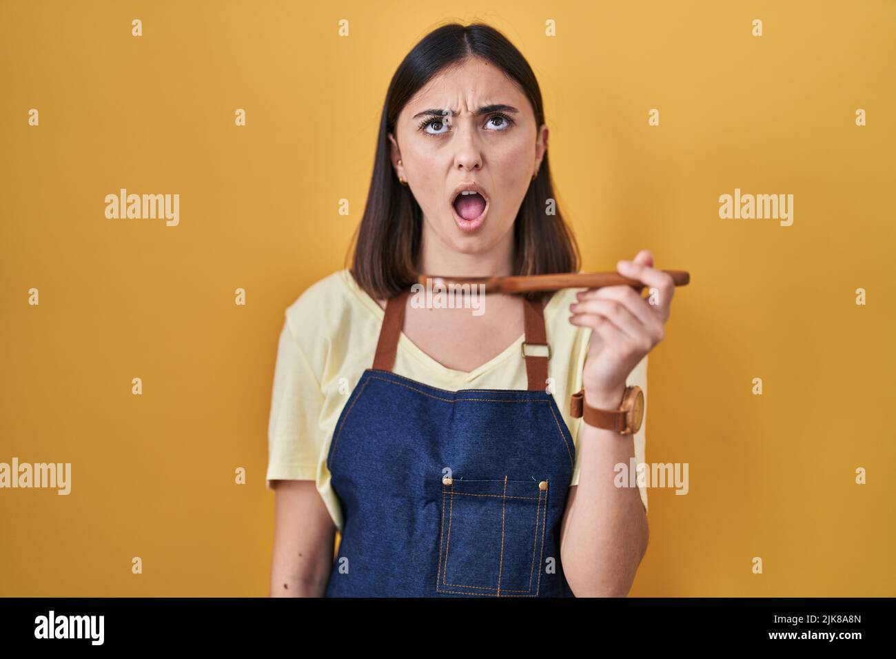 Hispanic girl eating healthy wooden spoon angry and mad screaming ...