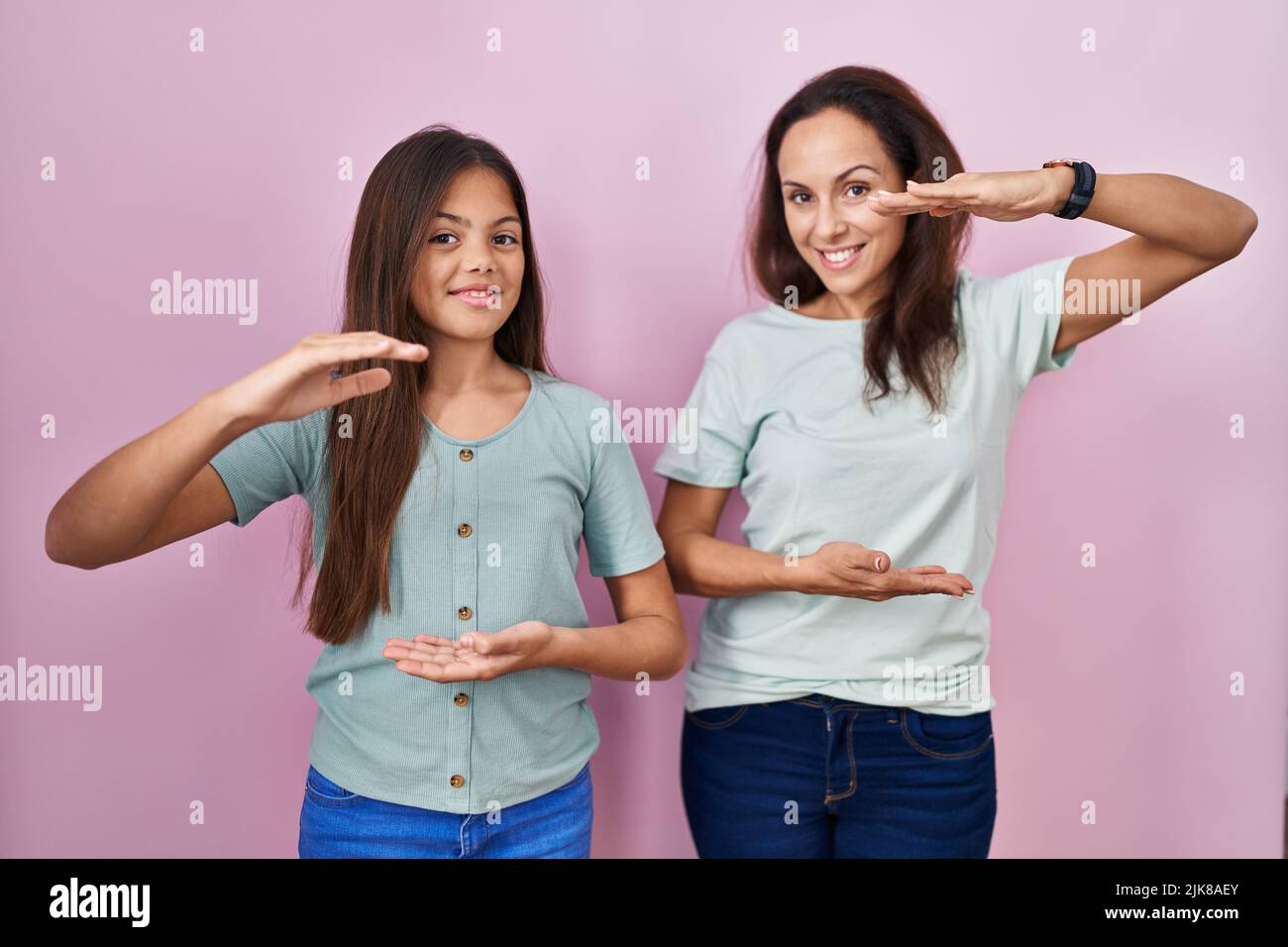 Young Mother And Daughter Standing Over Pink Background Gesturing With