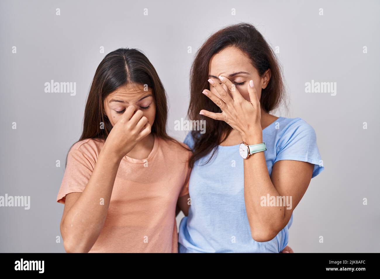 Young mother and daughter standing over white background tired rubbing ...