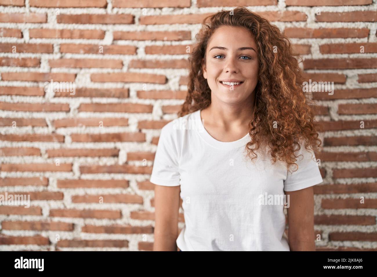 Young caucasian woman standing over bricks wall background with a happy ...