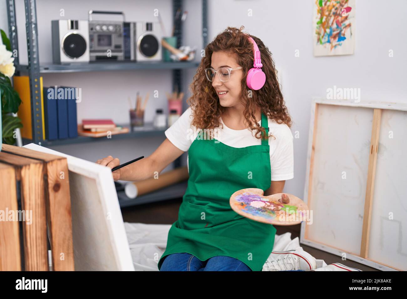 Young beautiful hispanic woman artist listening to music drawing at art ...