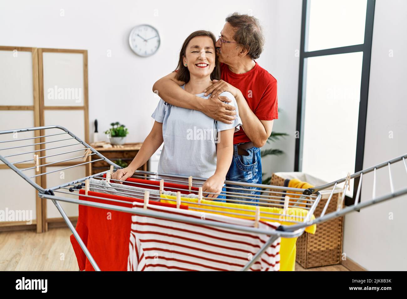 Middle age man and woman couple hugging and hanging clothes on ...