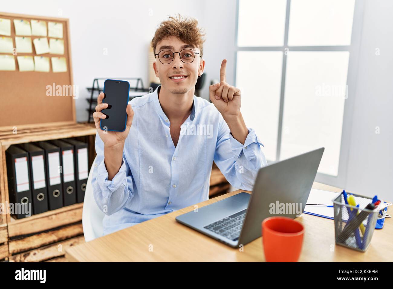 Young caucasian businessman working using laptop and showing smartphone ...