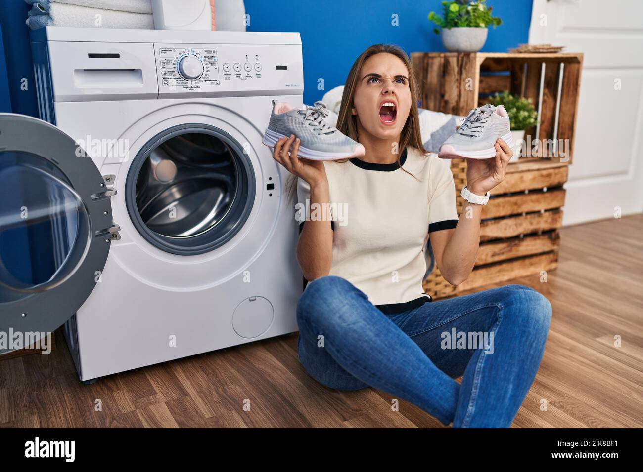 Young woman putting sneakers in washing machine angry and mad screaming ...