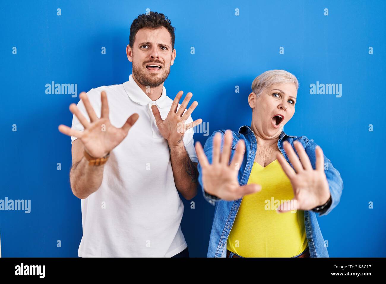 Young brazilian mother and son standing over blue background afraid and ...