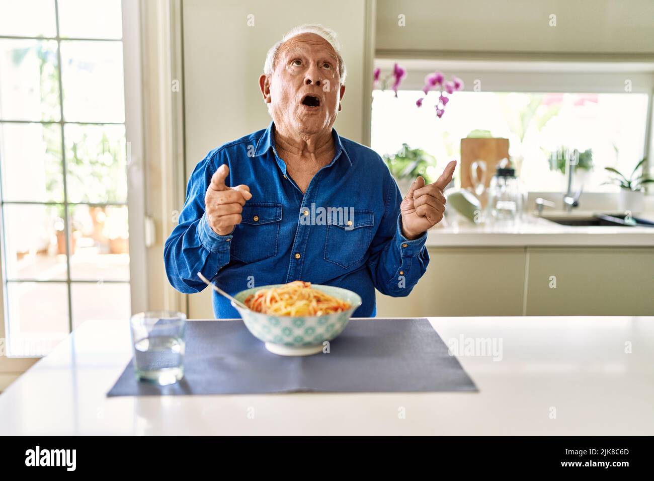 Senior man with grey hair eating pasta spaghetti at home amazed and ...