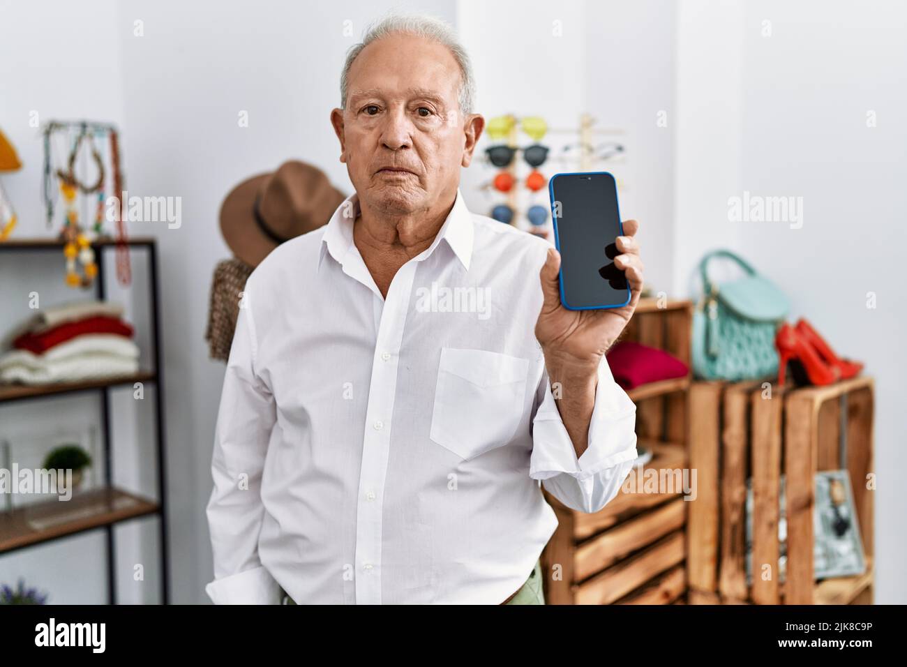 Senior man holding smartphone at retail shop thinking attitude and ...