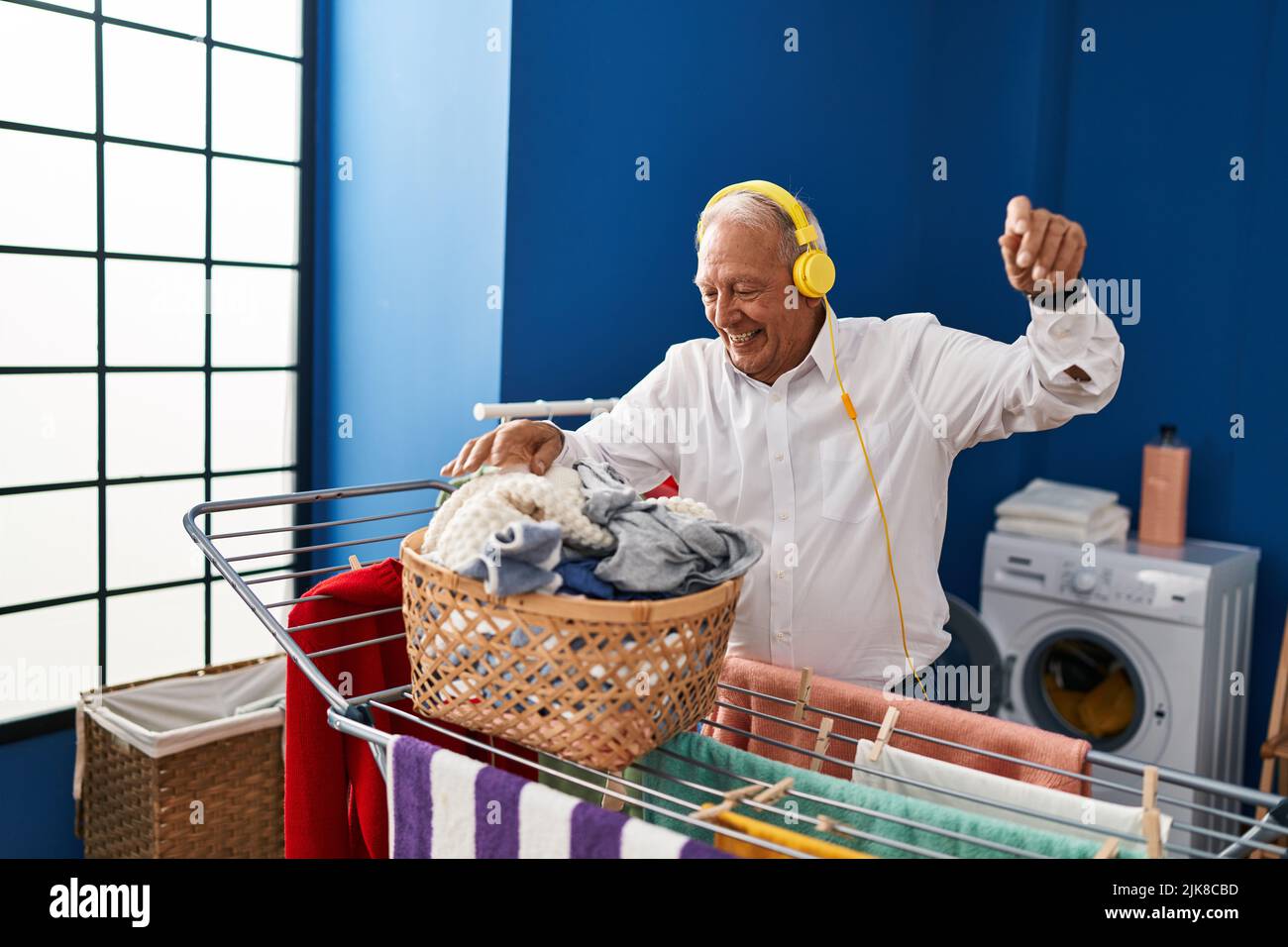 Senior man listening to music hanging clothes on clothesline at laundry ...