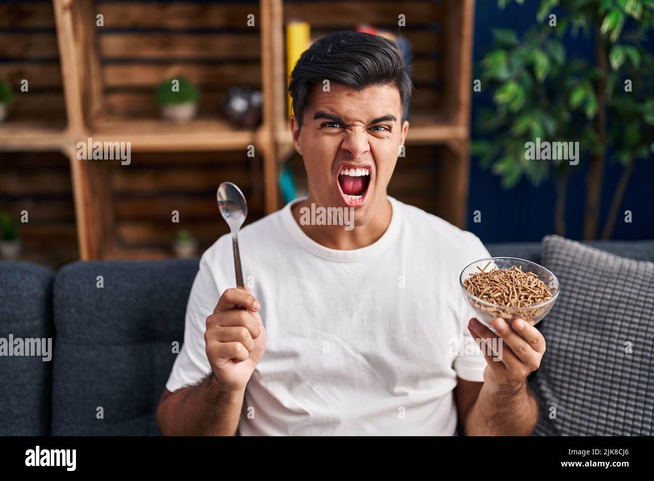 Hispanic man eating healthy whole grain cereals with spoon angry and ...