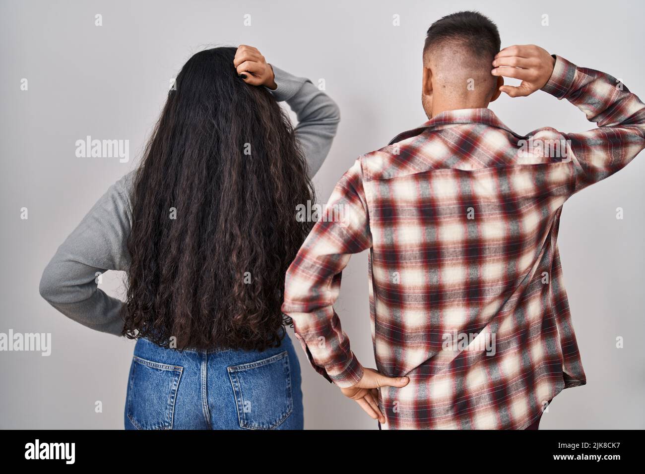 Young hispanic couple standing over white background backwards thinking ...