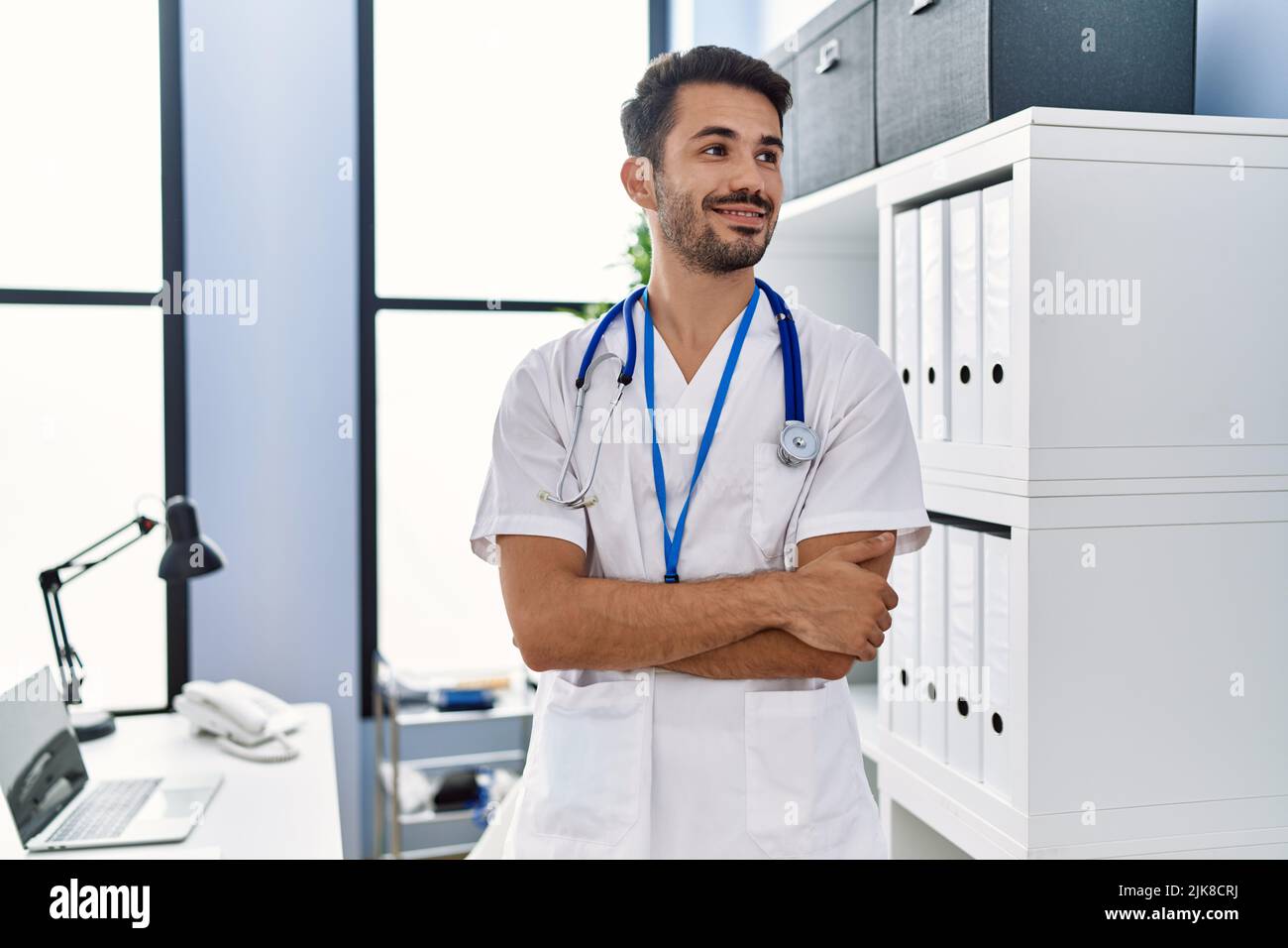 Young hispanic man wearing doctor uniform standing with arms crossed ...