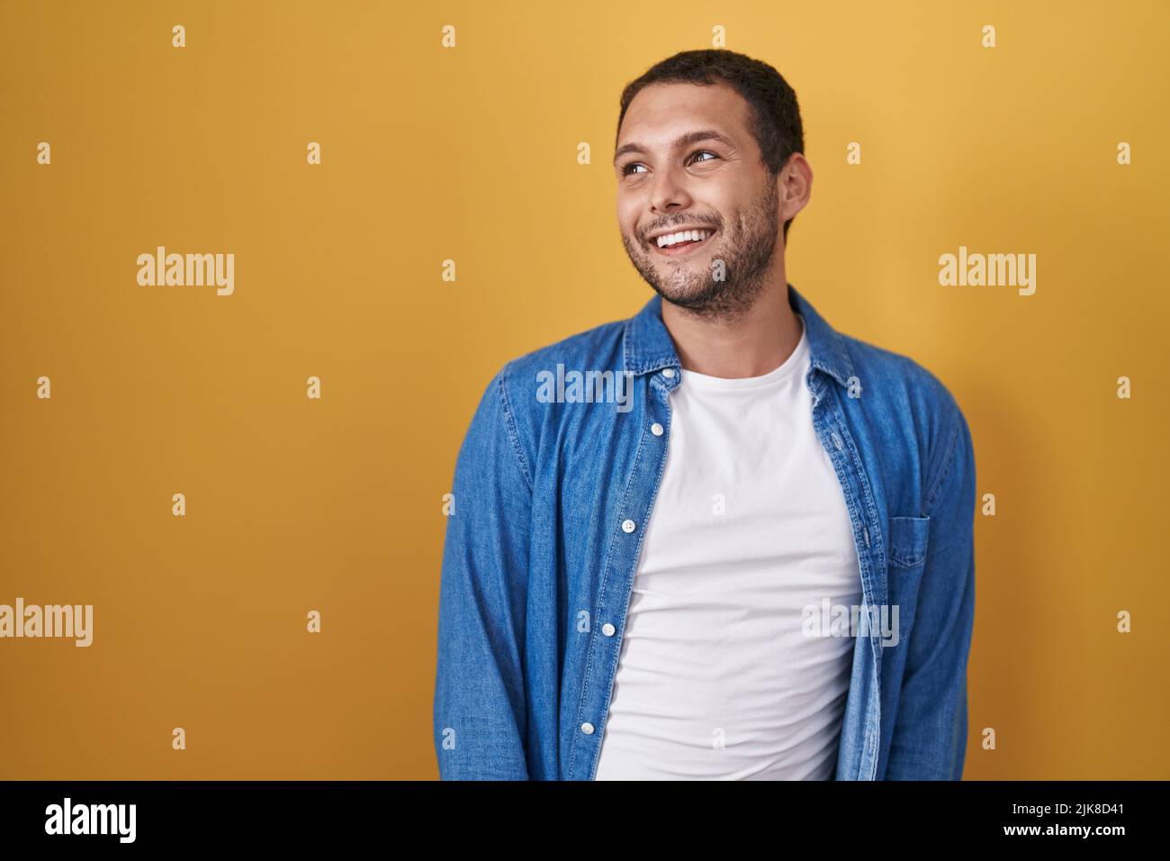 Hispanic man standing over yellow background looking away to side with ...