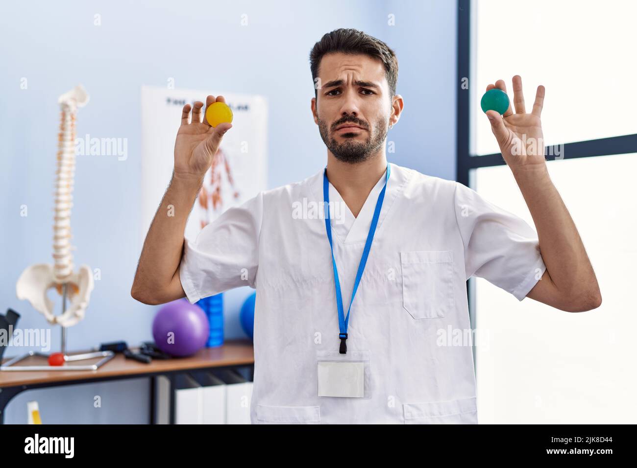 Young hispanic physiotherapist man holding strength balls to train hand ...