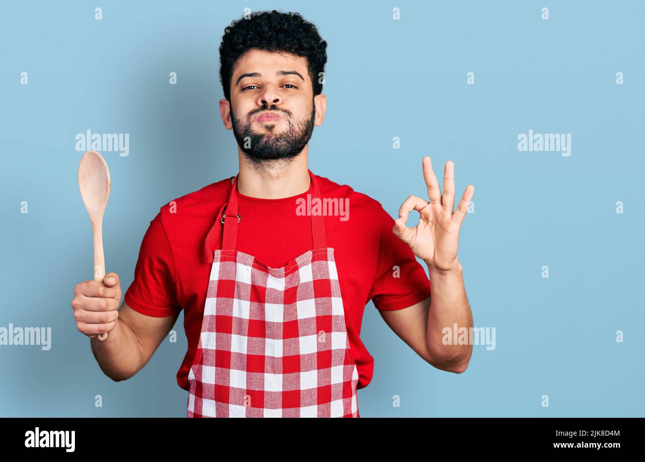 Young arab man with beard wearing baker uniform holding wooden spoon ...