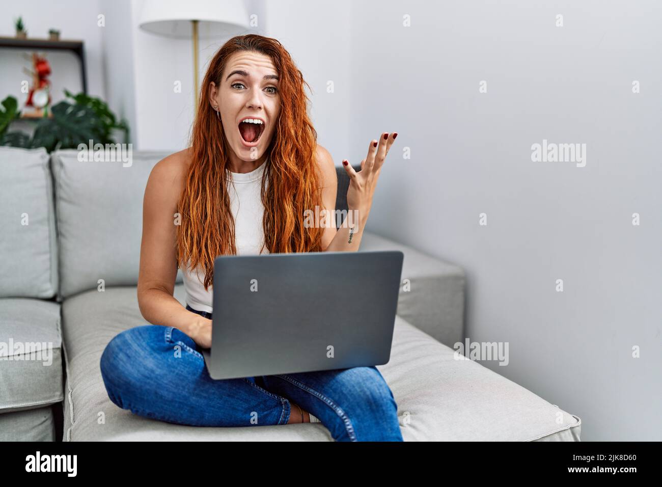 Young redhead woman using laptop at home celebrating victory with happy ...