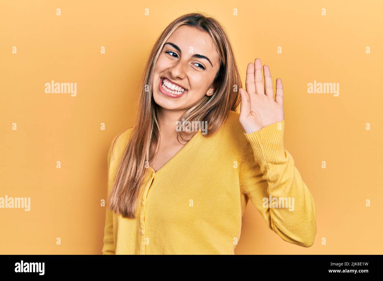 Beautiful hispanic woman wearing casual yellow sweater waiving saying ...