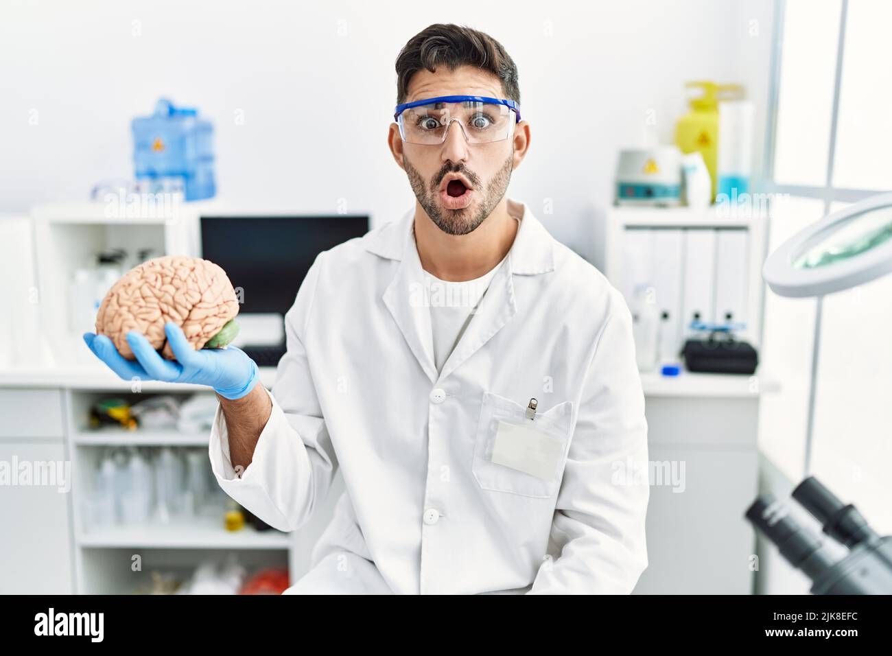 Young hispanic man working at laboratory holding medical brain scared ...