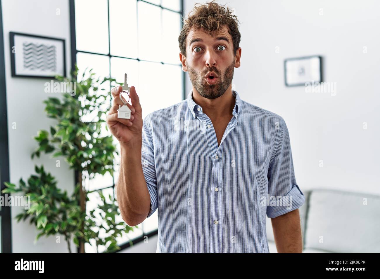 Young handsome man holding keys of new home scared and amazed with open ...