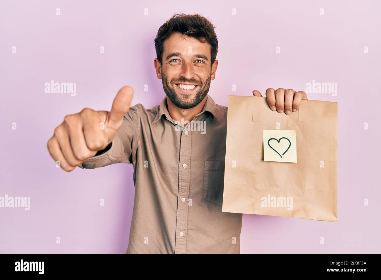 Handsome man with beard holding delivery paper bag with heart reminder ...