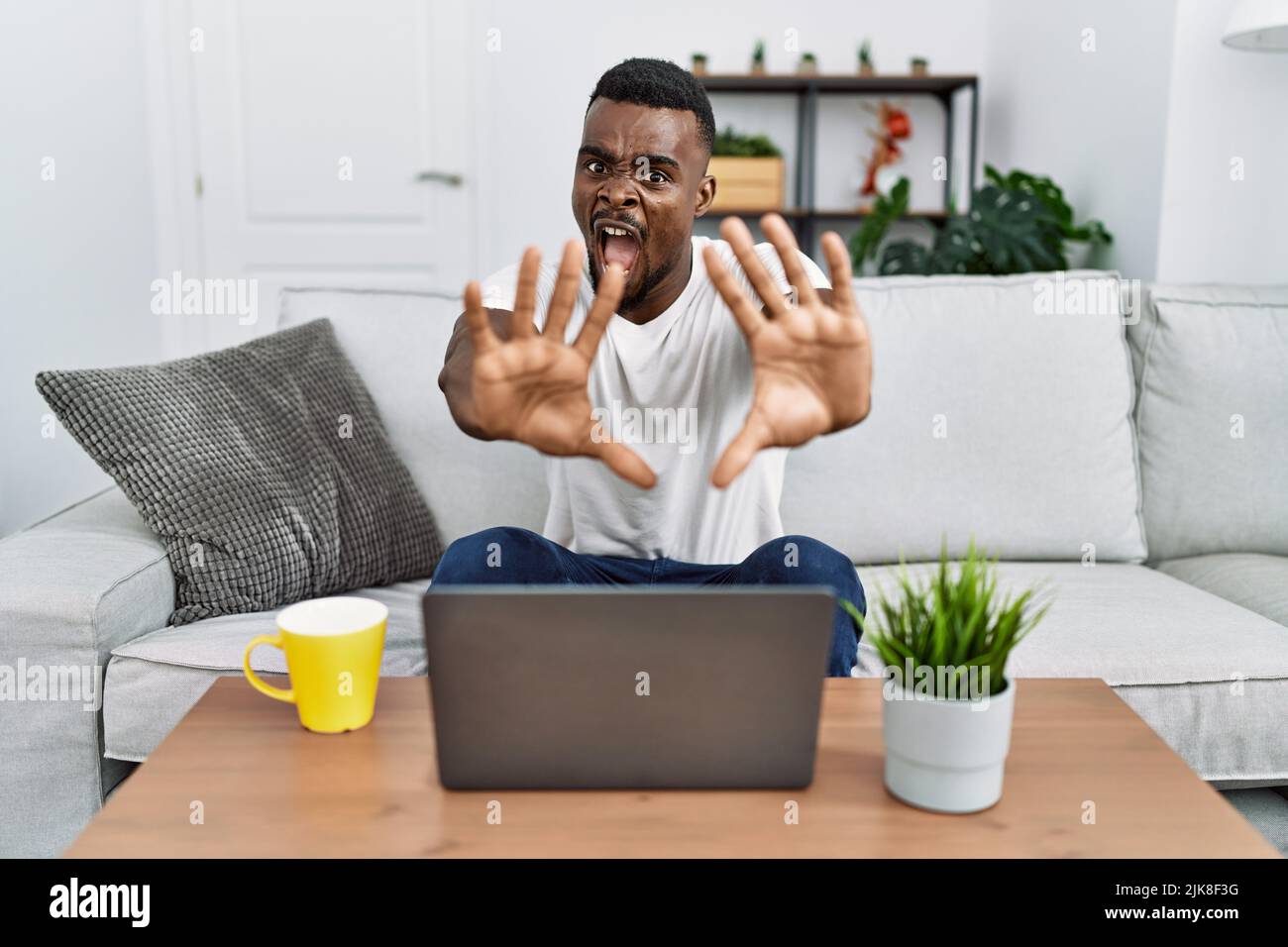 Young african man using laptop at home afraid and terrified with fear ...