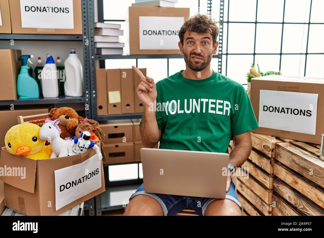 Young handsome man wearing volunteer t shirt using laptop pointing ...