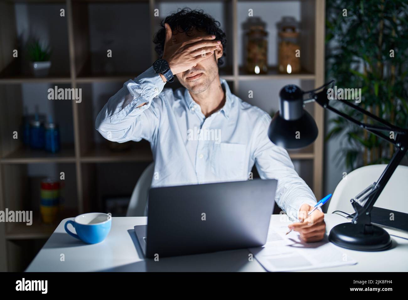Hispanic man working at the office at night smiling and laughing with ...