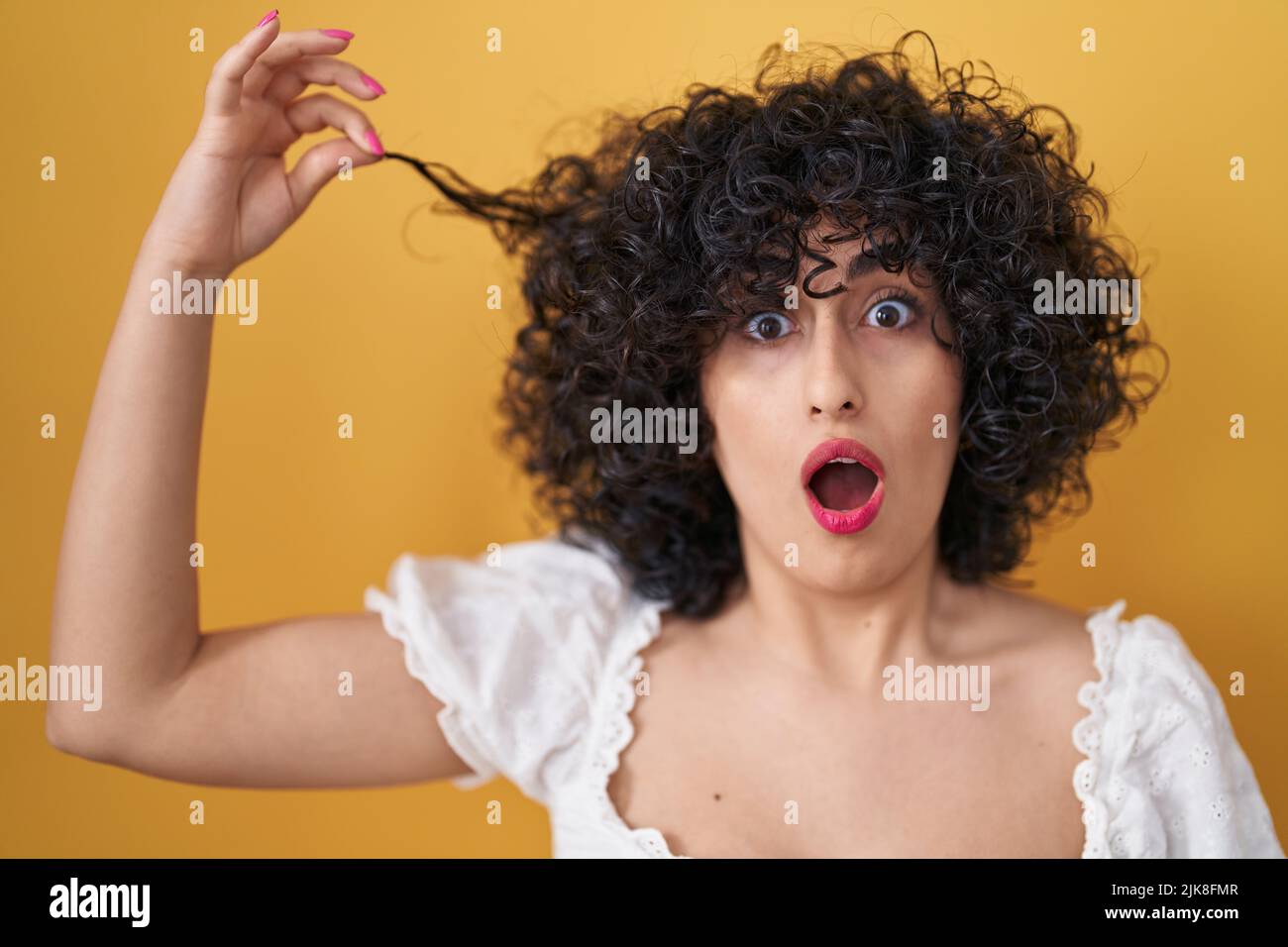 Young brunette woman with curly hair holding curl afraid and shocked ...