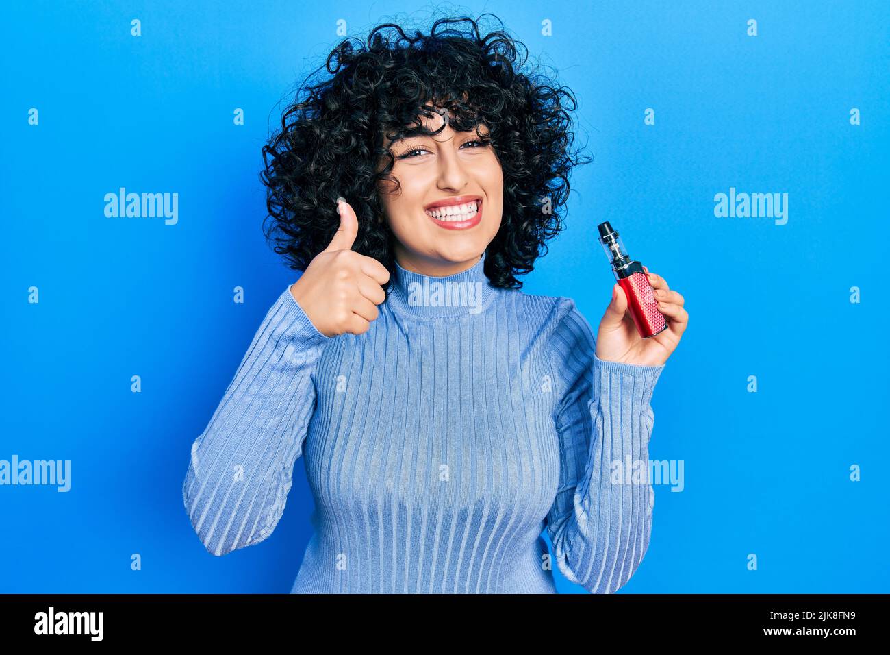 Young middle east woman holding electronic cigarette smiling happy and ...