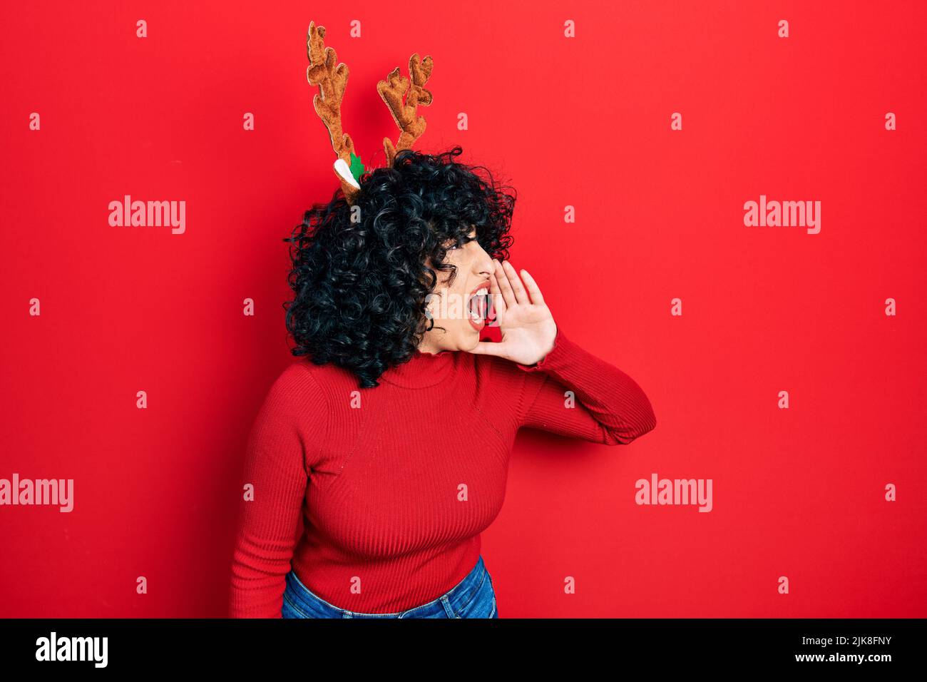 Young middle east woman wearing cute christmas reindeer horns shouting ...
