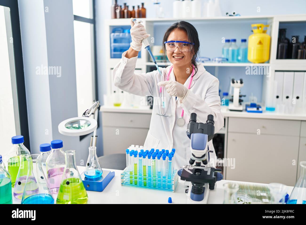 Young chinese woman wearing scientist uniform working at laboratory ...