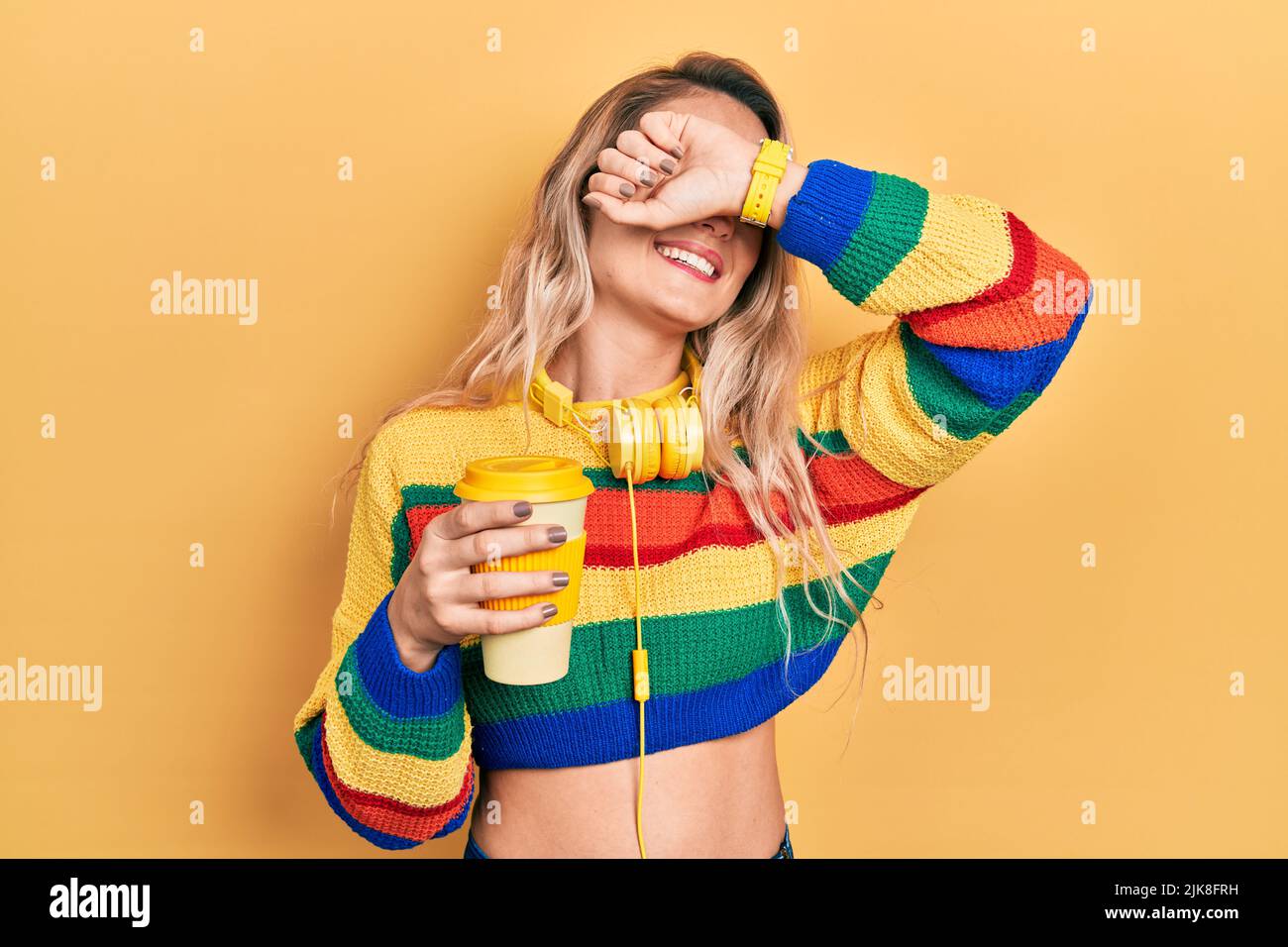 Beautiful young blonde woman drinking cup of coffee wearing headphones ...