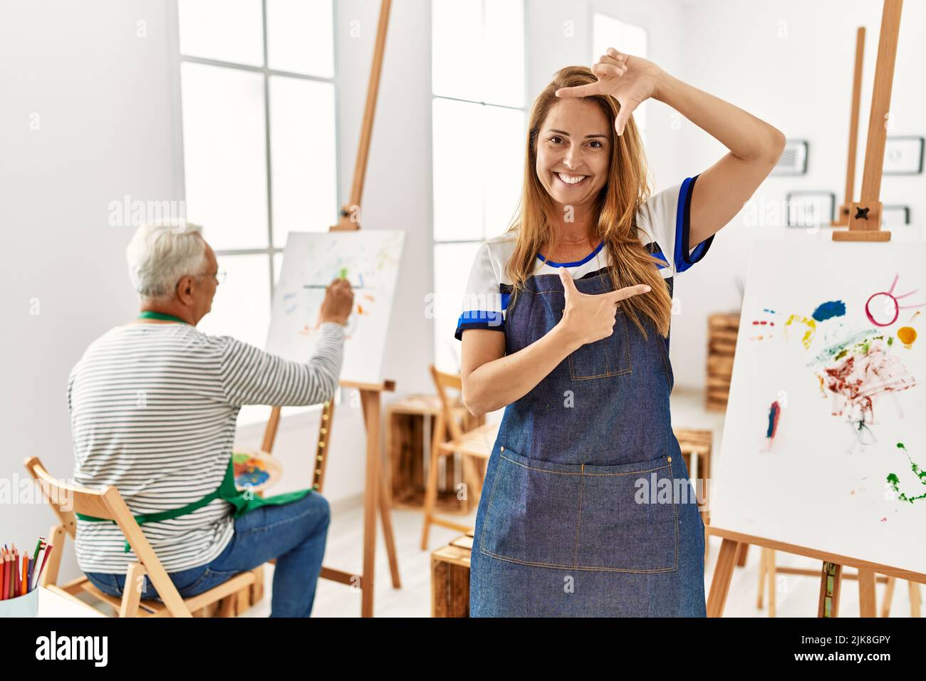 Hispanic woman wearing apron at art studio smiling making frame with ...